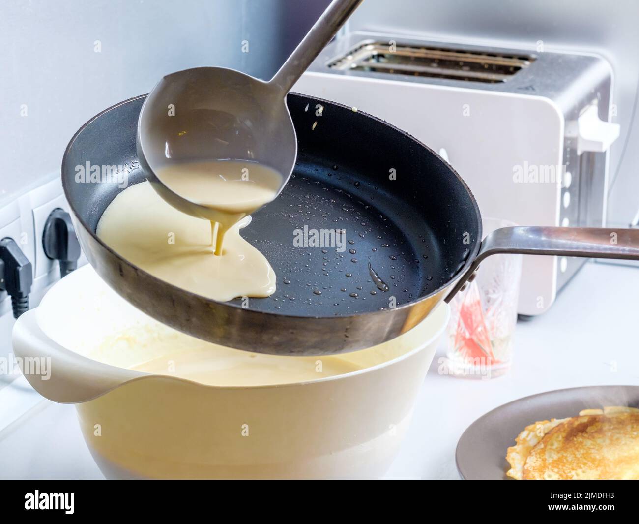 Batter pouring out of a metal bucket onto a red-hot greased frying pan ...