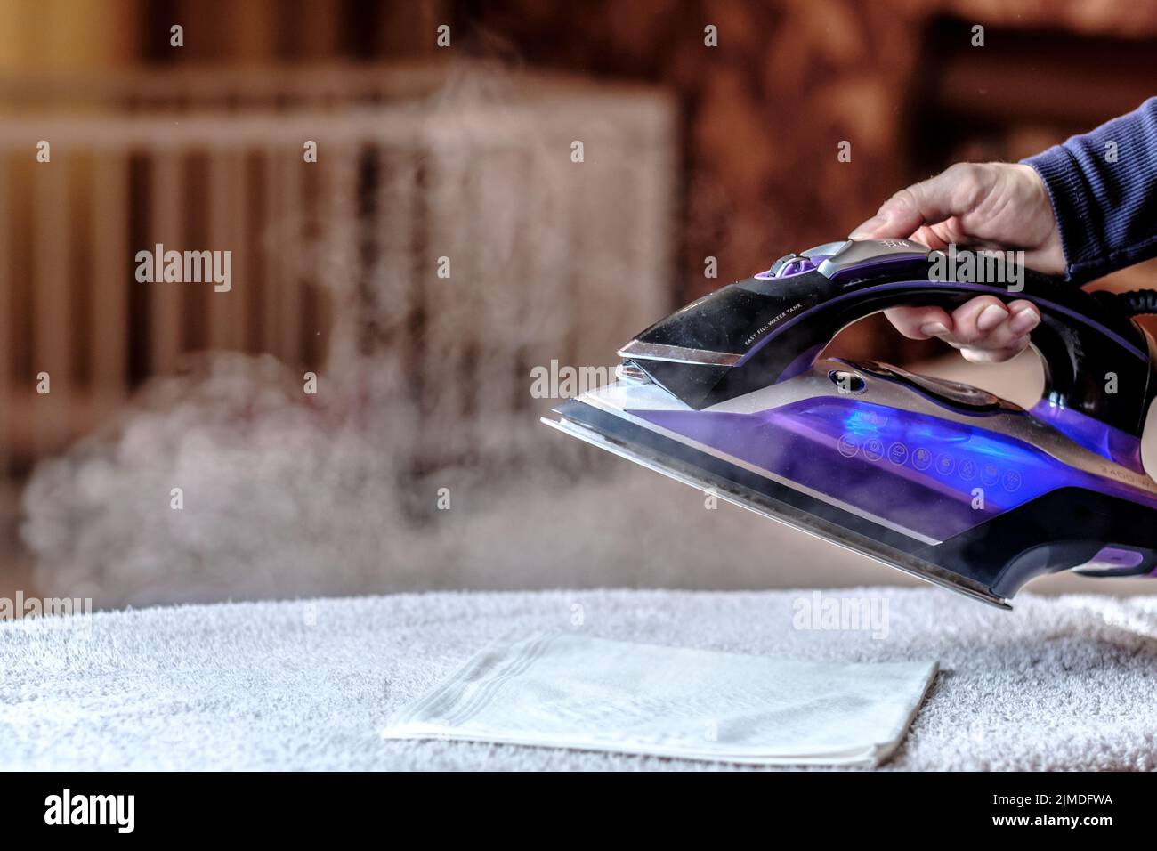 Closeup female hand ironing clothes on the table. Puffs of hot steam ...