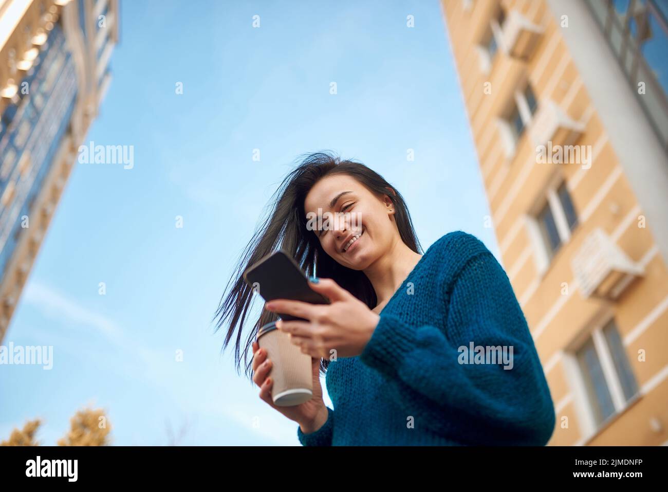 Charming model posing with a cellphone opposite modern towers and sky ...