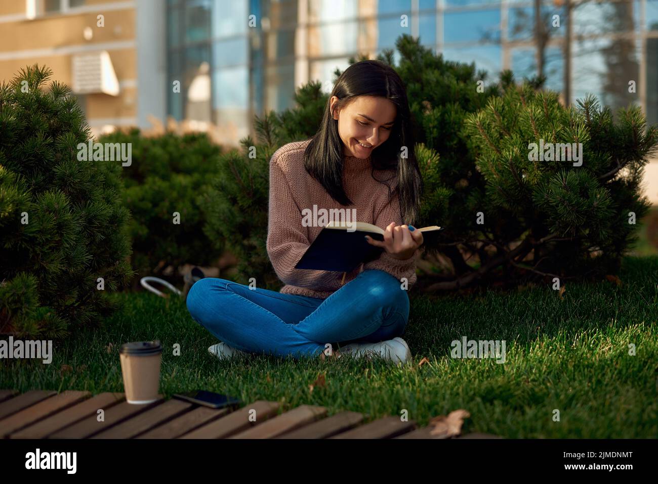 Charming female enjoys reading sitting on a lawn in the yard of an ...