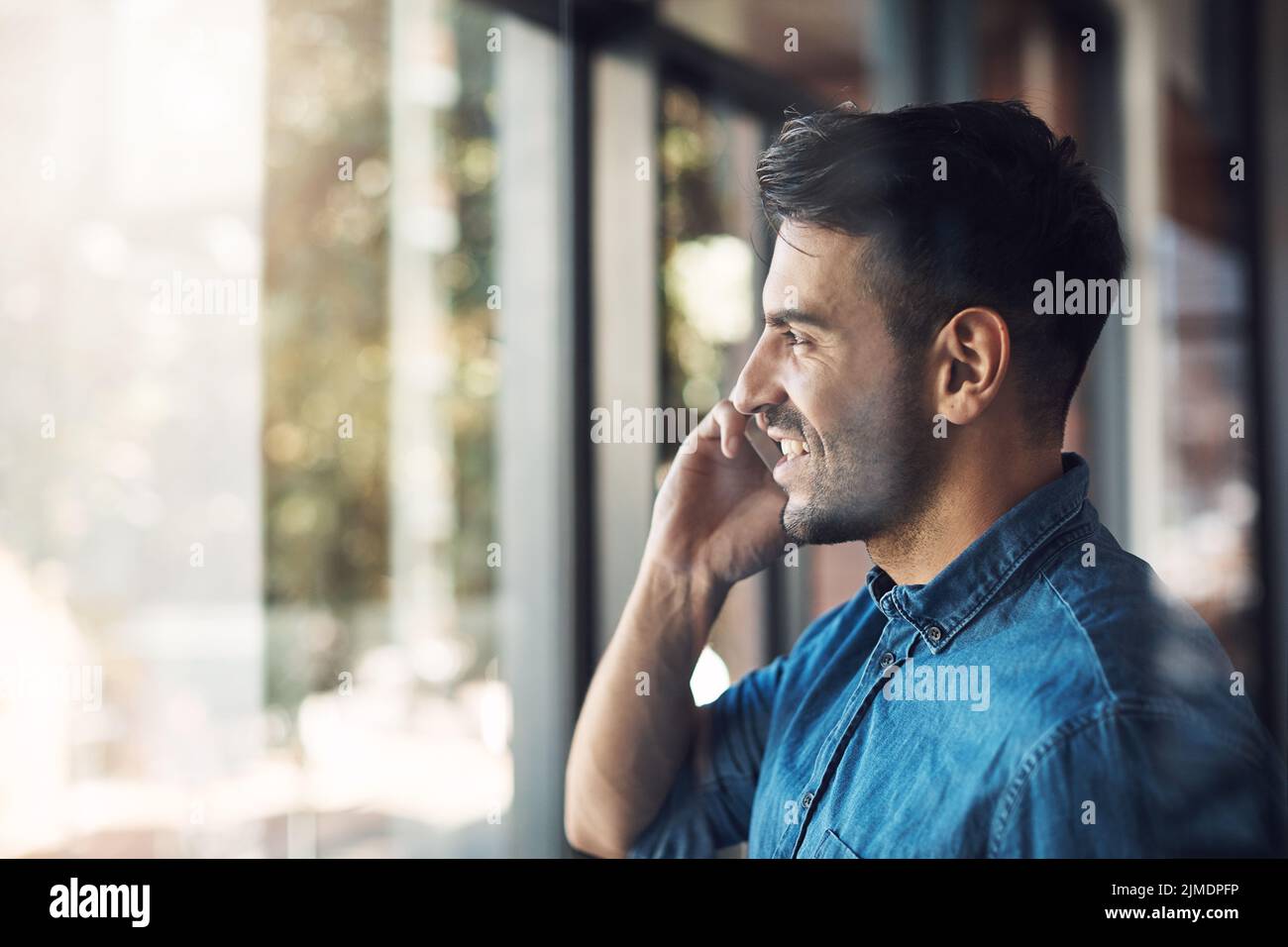 Smiling casual man on a phone call looking out a window indoors. Happy ...