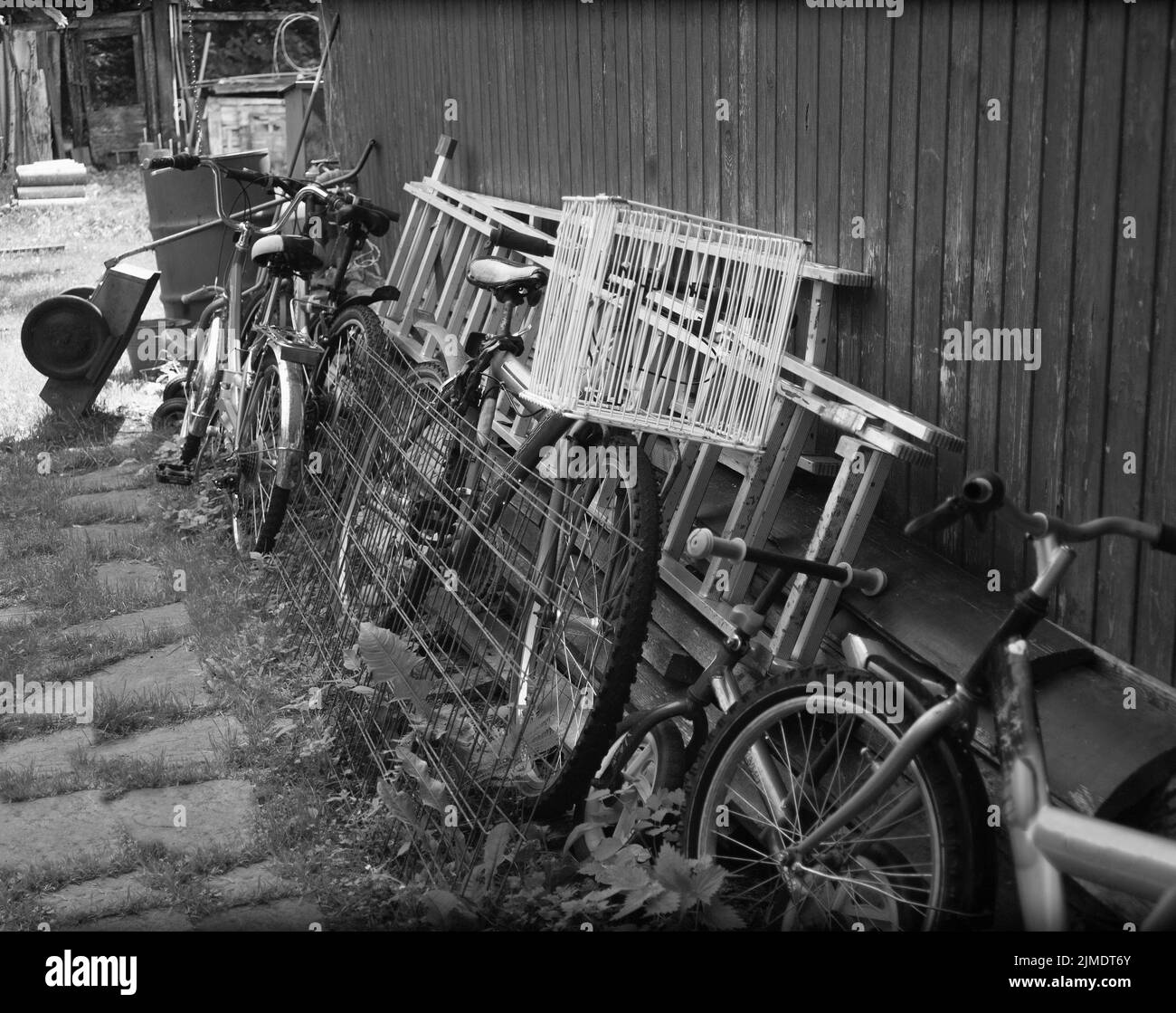 collection of used bikes leaned against the wall in a messy backyard, in black and white Stock ...