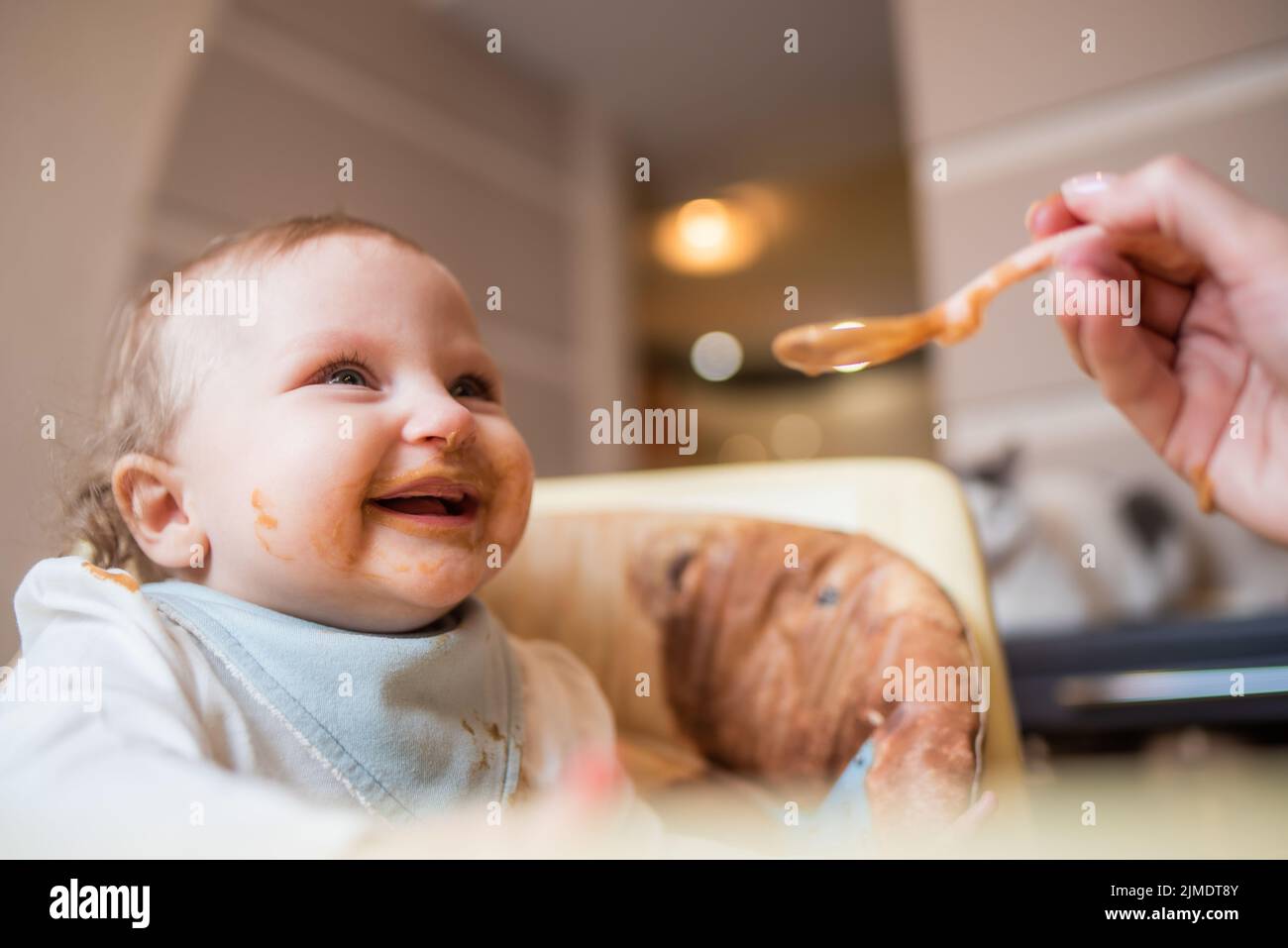 Happy mother feeding her cute little daughter fruit puree from spoon at ...
