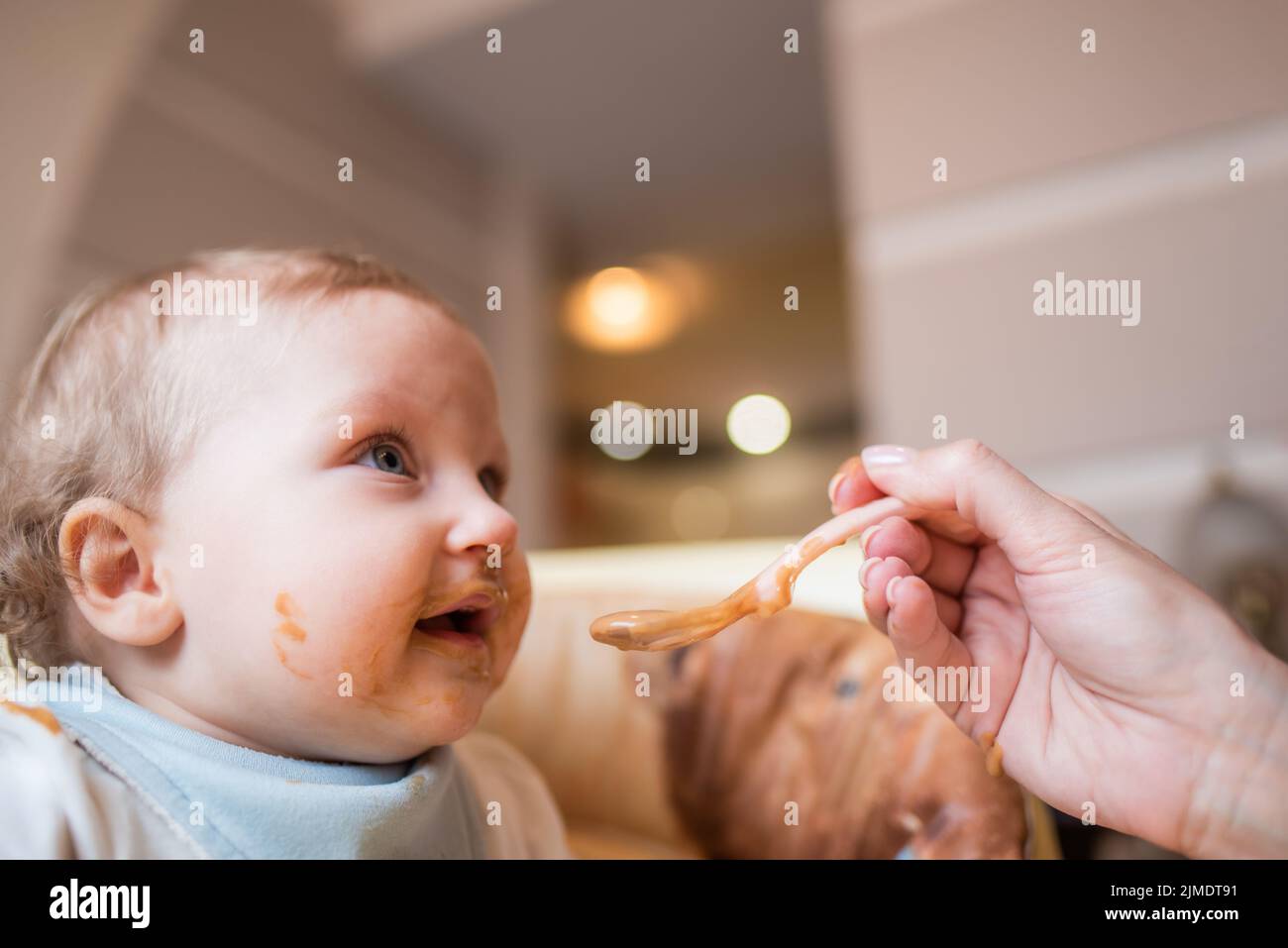 Happy mother feeding her cute little daughter fruit puree from spoon at ...