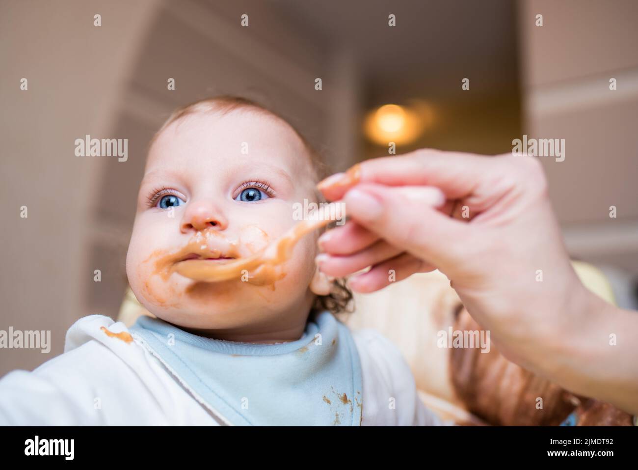 Happy mother feeding her cute little daughter fruit puree from spoon at ...