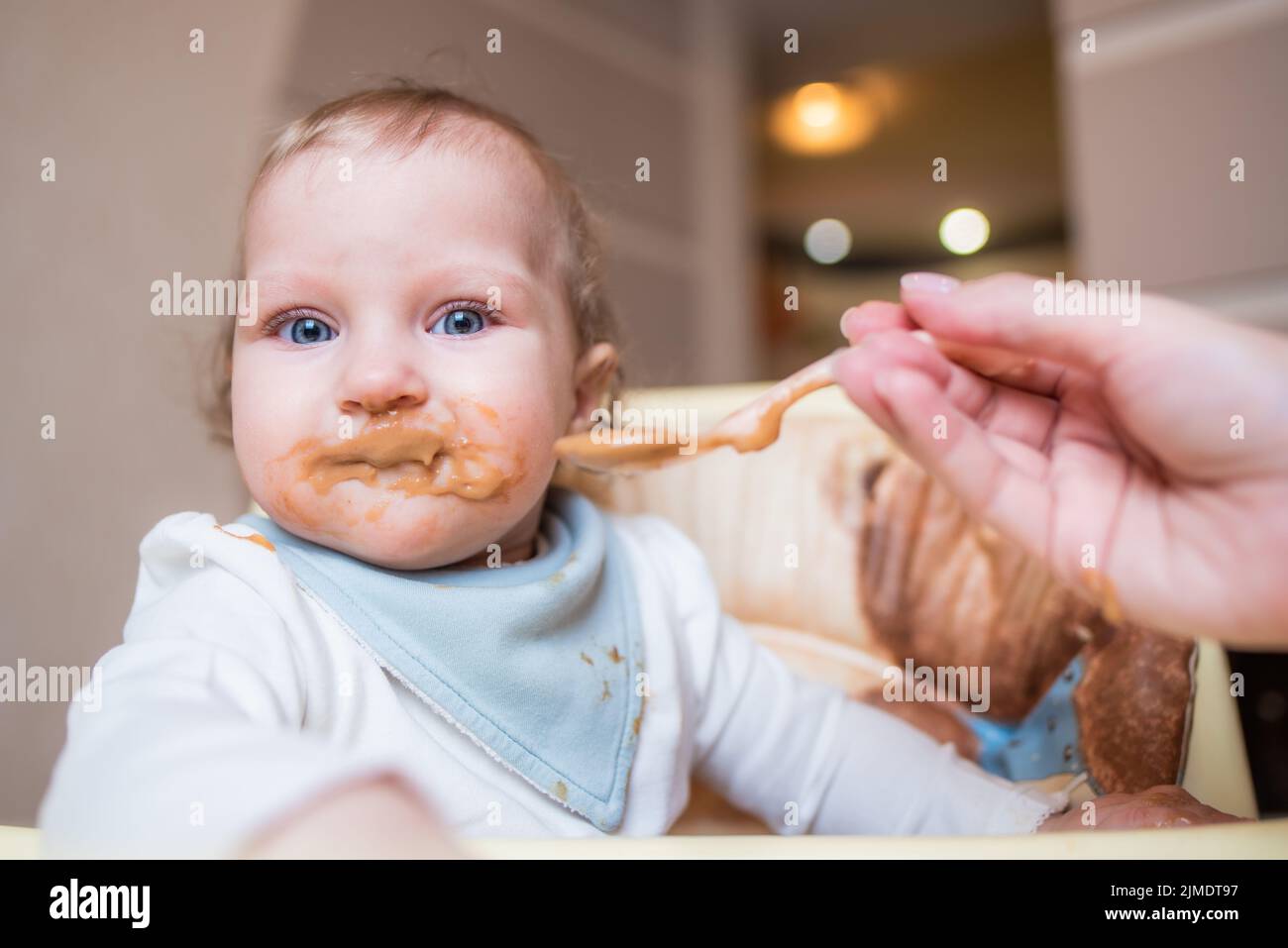 Happy mother feeding her cute little daughter fruit puree from spoon at ...