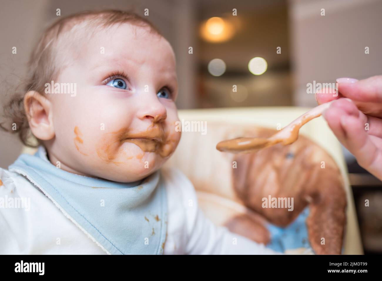 Happy mother feeding her cute little daughter fruit puree from spoon at ...