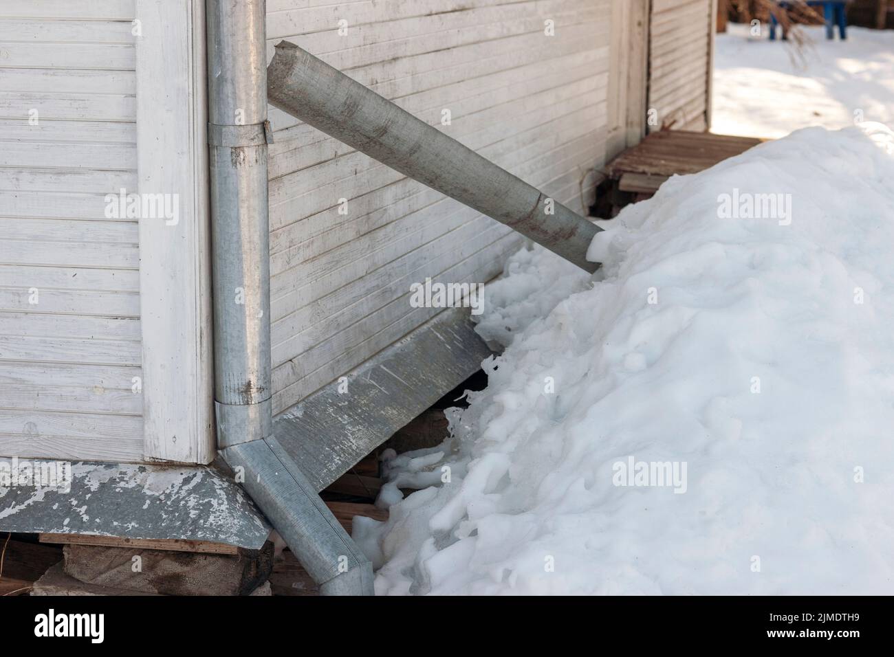 a building with damaged metal downspout downed on the ground, winter ...