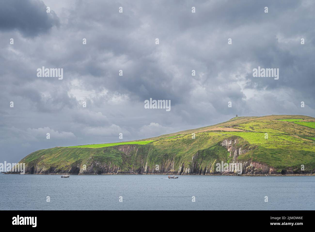 Fishing boats returning to Dingle village with green fields on tall ...