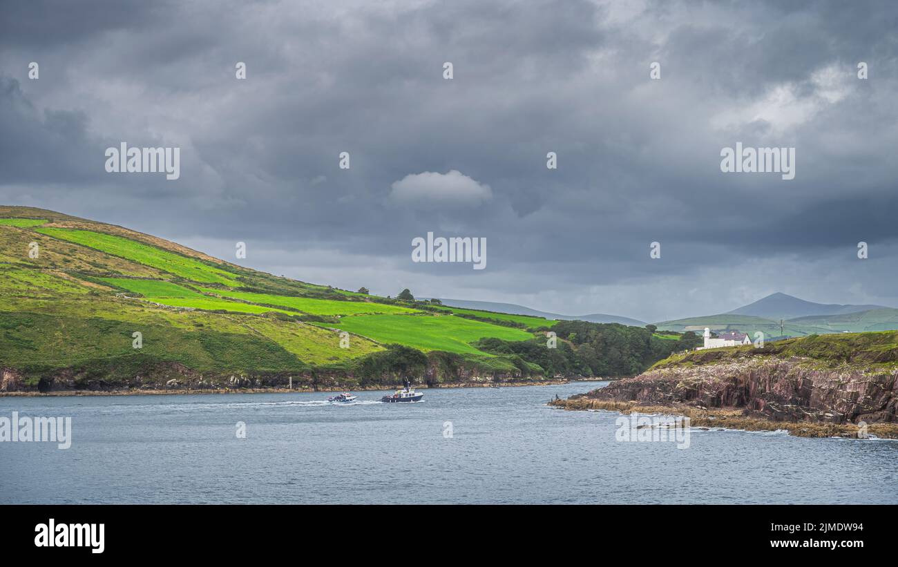 Fishing or tour boats returning to Dingle harbour guided by lighthouse ...