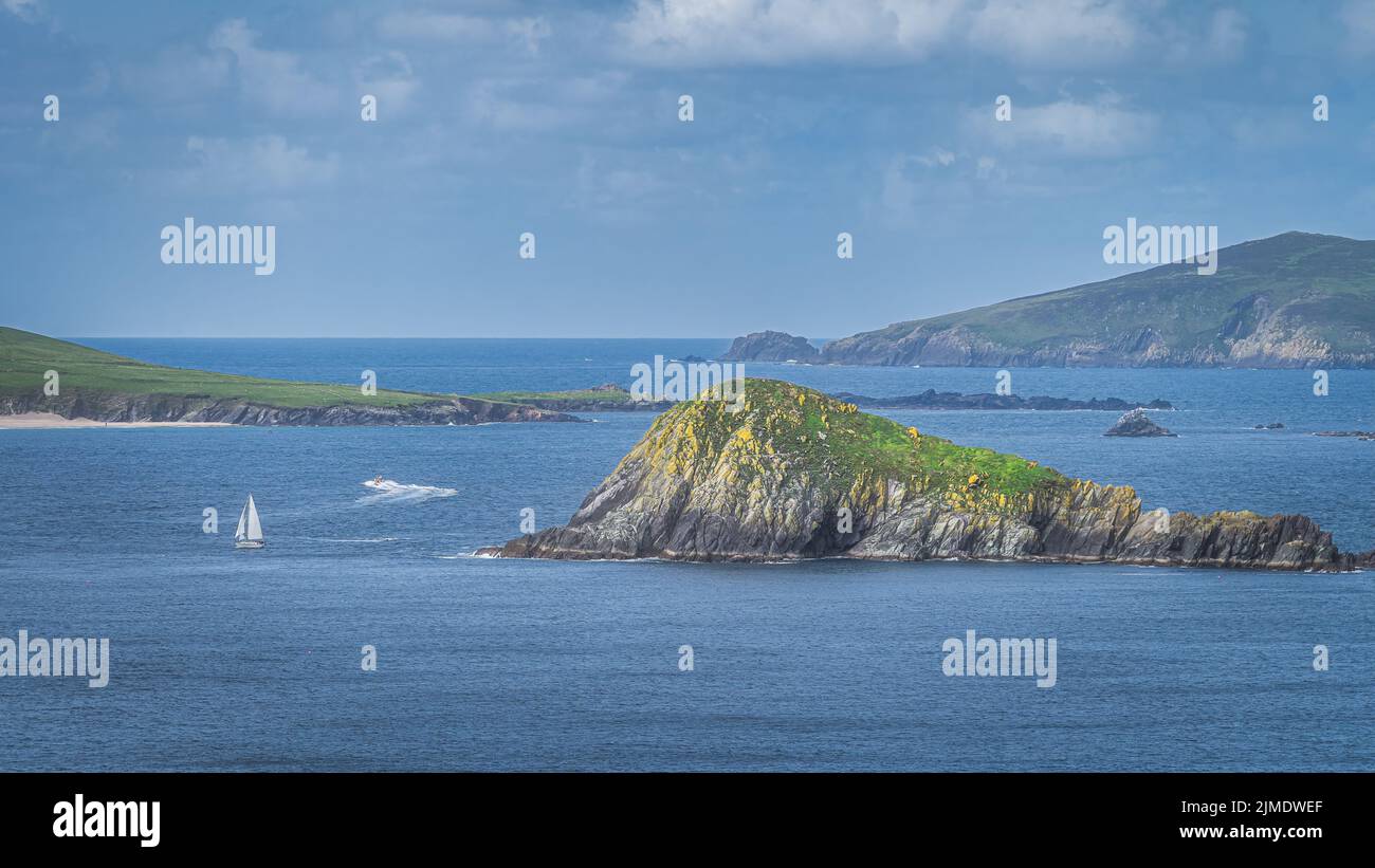 Sailboat and motorboat sailing between small rocky islands in Dingle ...