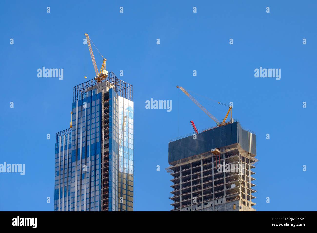 Tower cranes atop an unfinished skyscraper against a clear blue sky ...