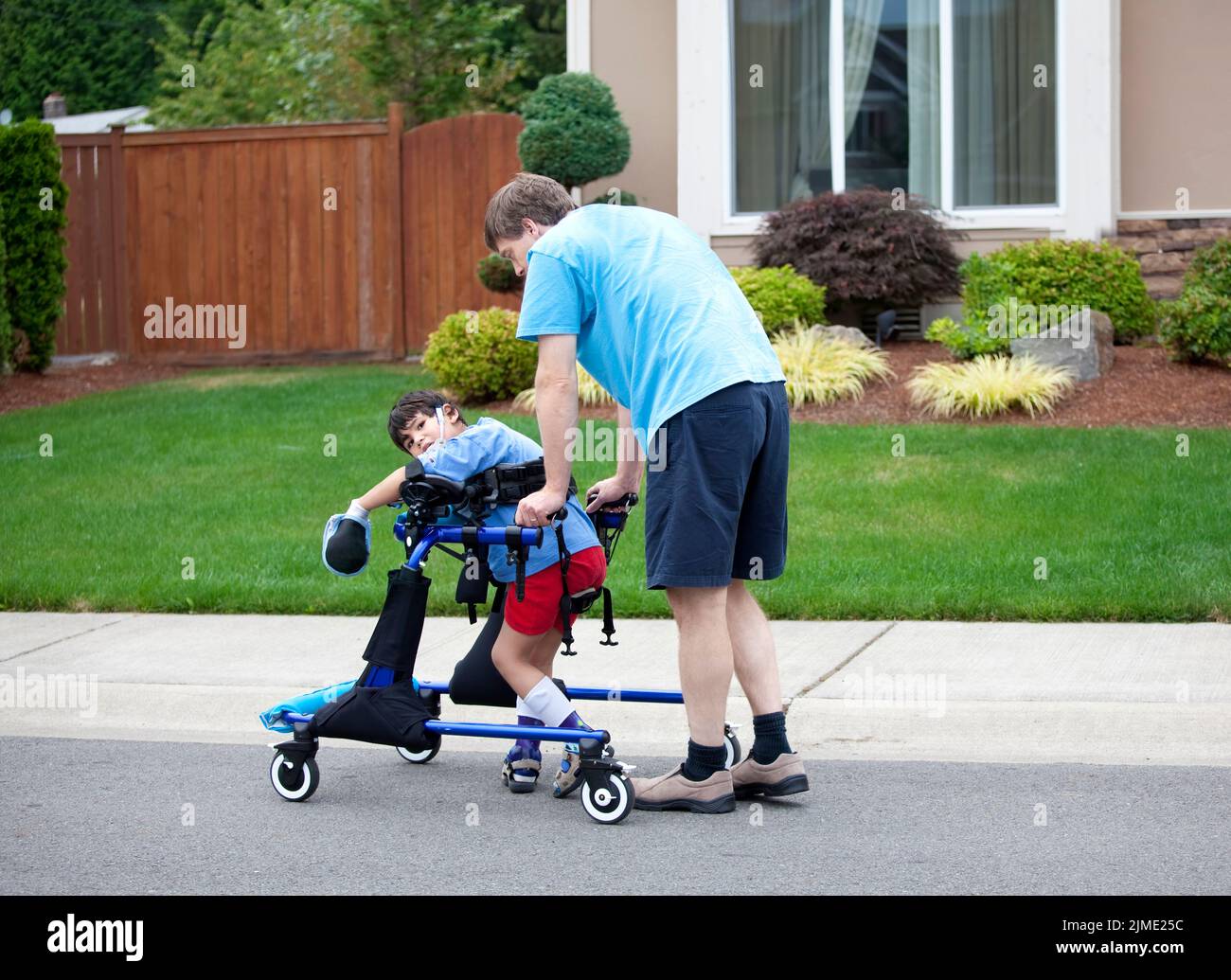Father helping disabled son walk in his walker outdoors on road Stock ...