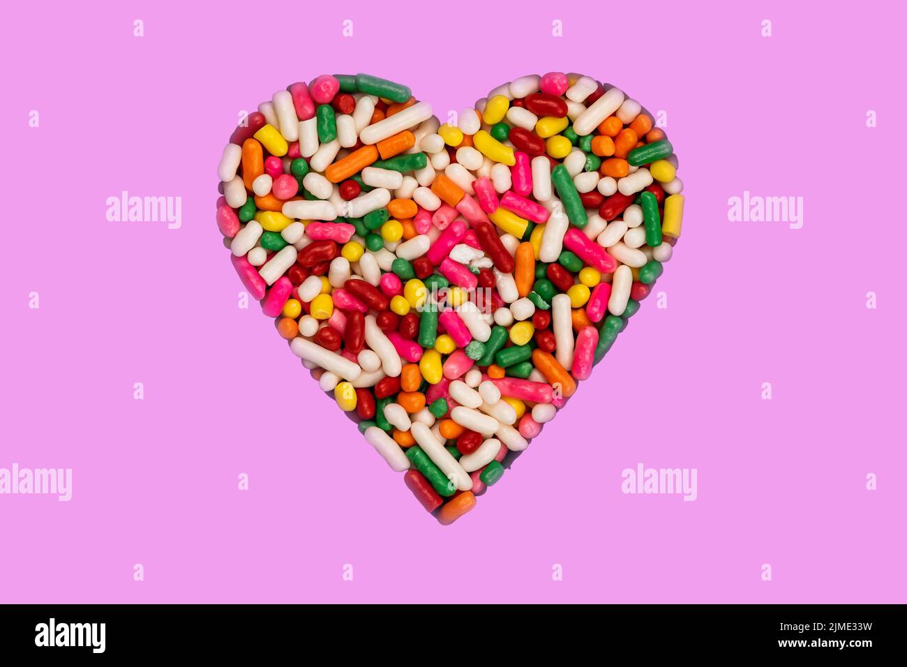 Heart shaped colorful rainbow sprinkles isolated on pink background ...