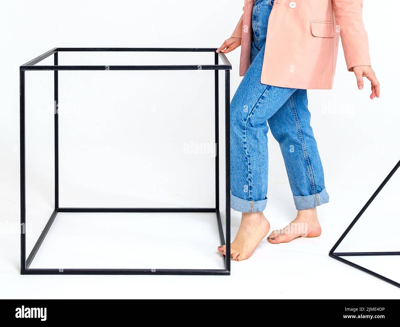 A barefoot young woman stands next to a skeleton of a cube on a white ...