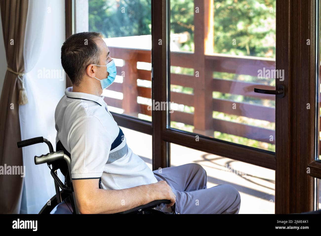 Young man wearing face mask sitting in a wheelchair alone looking out ...