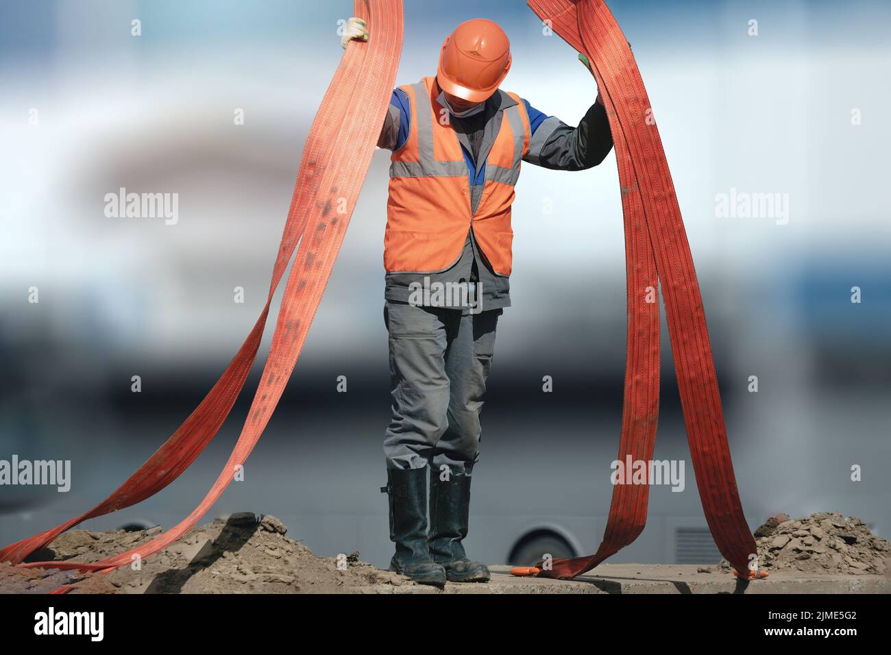 A slinger in a helmet and overalls works outside on a sunny day ...