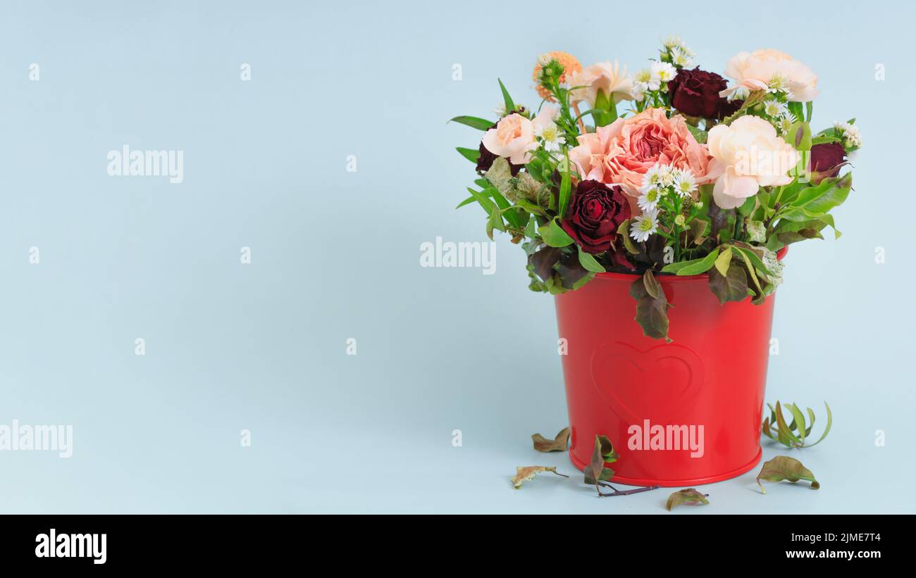This is a bouquet of withering flowers in a decorative bucket on a blue ...