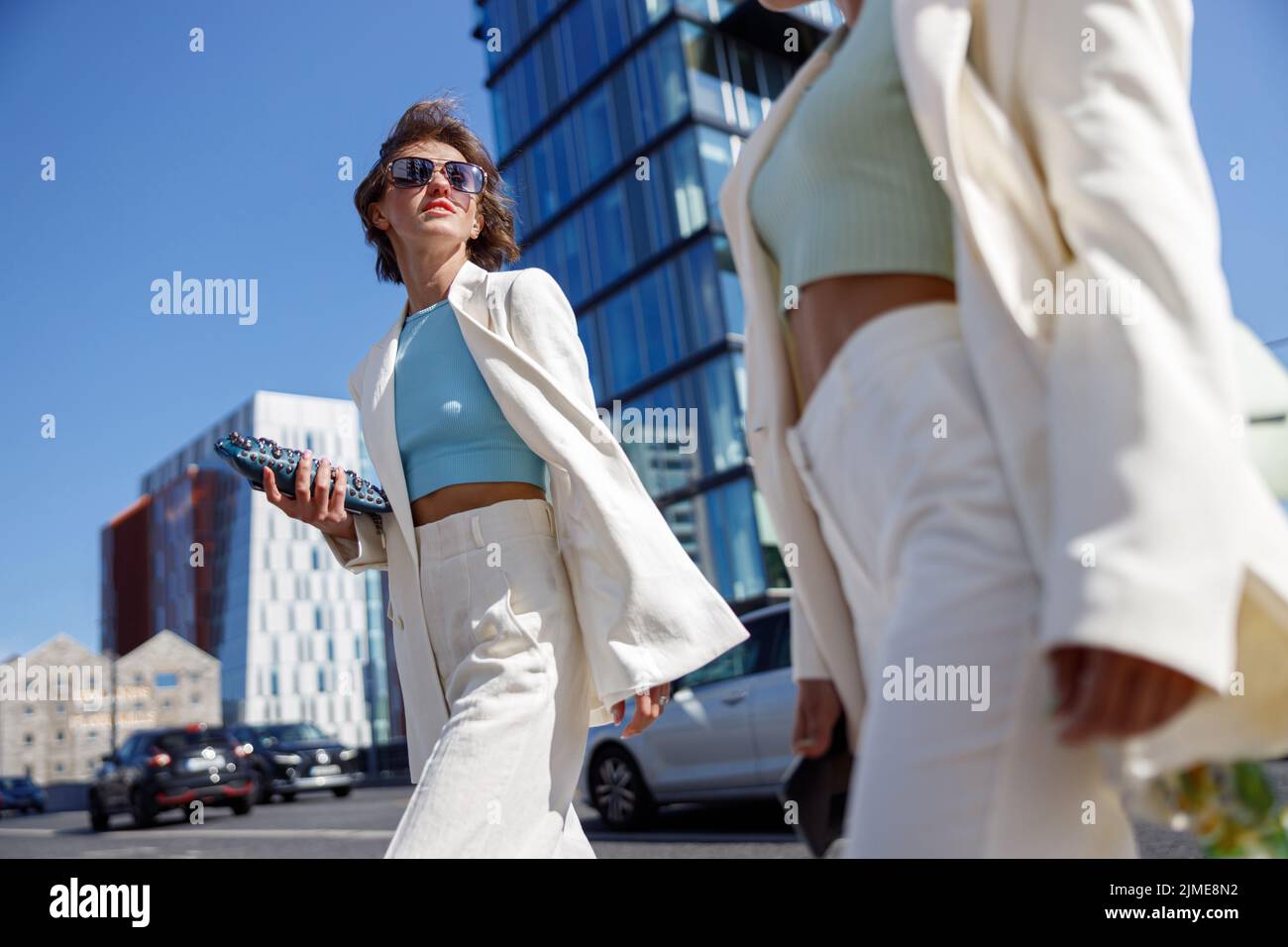 Two happy woman in trendy outfits laugh and walk outside on background ...
