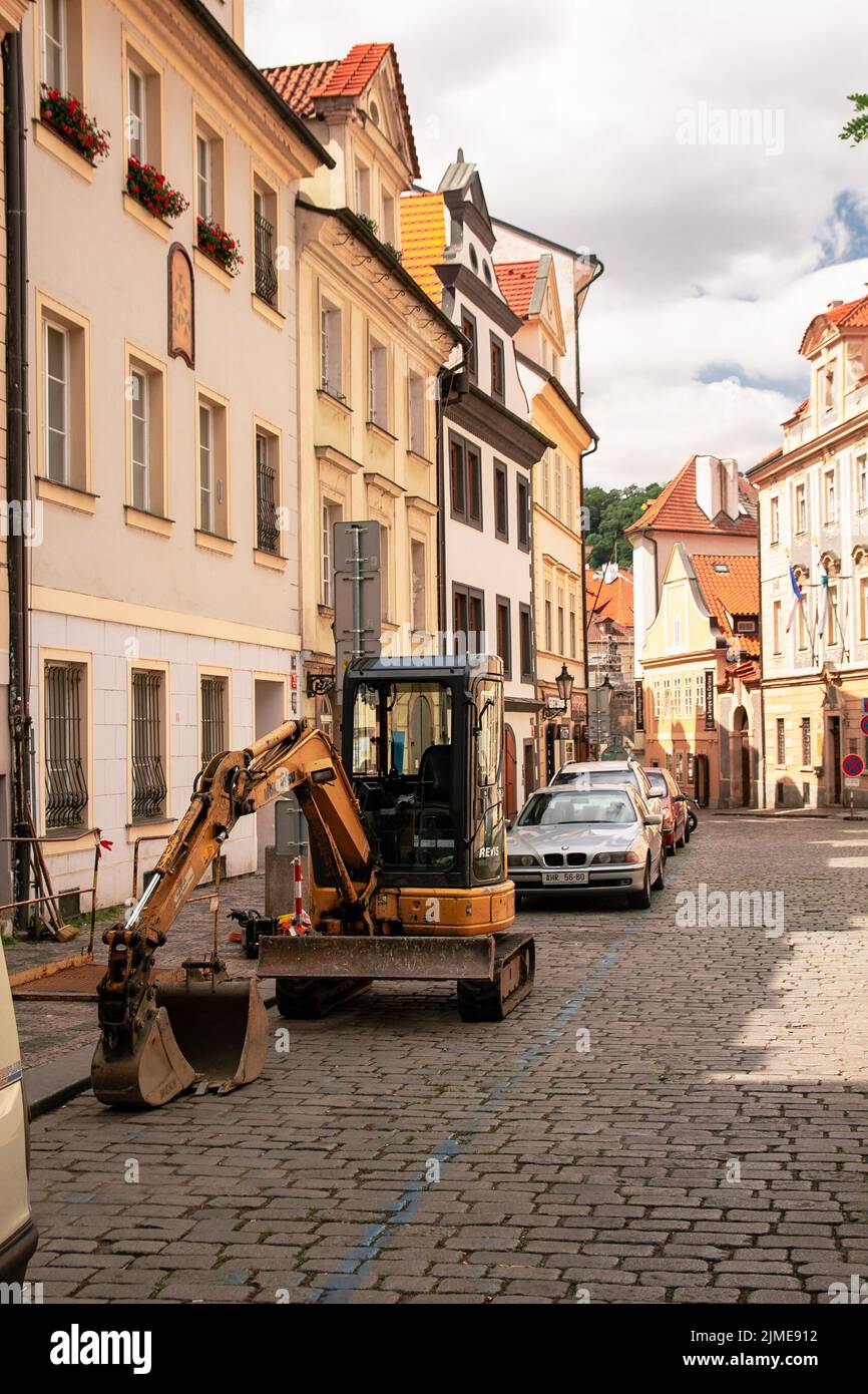 An excavator parked in an old-looking street in Prague between cars on ...