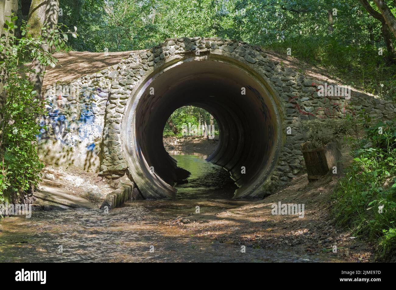 Little river flows in a pipe under the bridge Stock Photo - Alamy