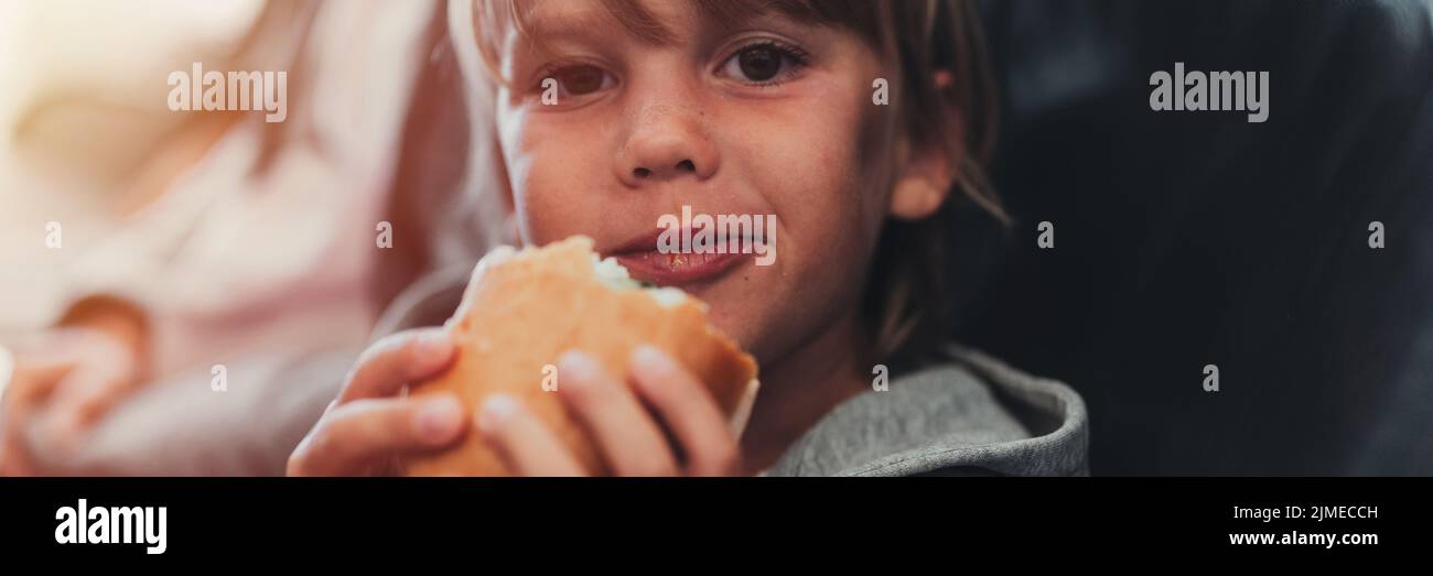 little candid kid boy five year old eats burger or sandwich food ...