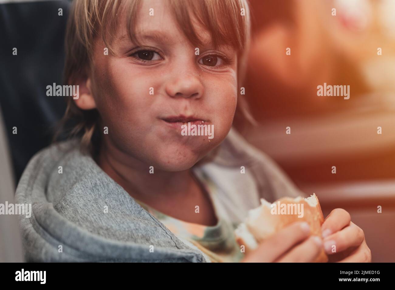 little candid kid boy five years old eats burger or sandwich food ...
