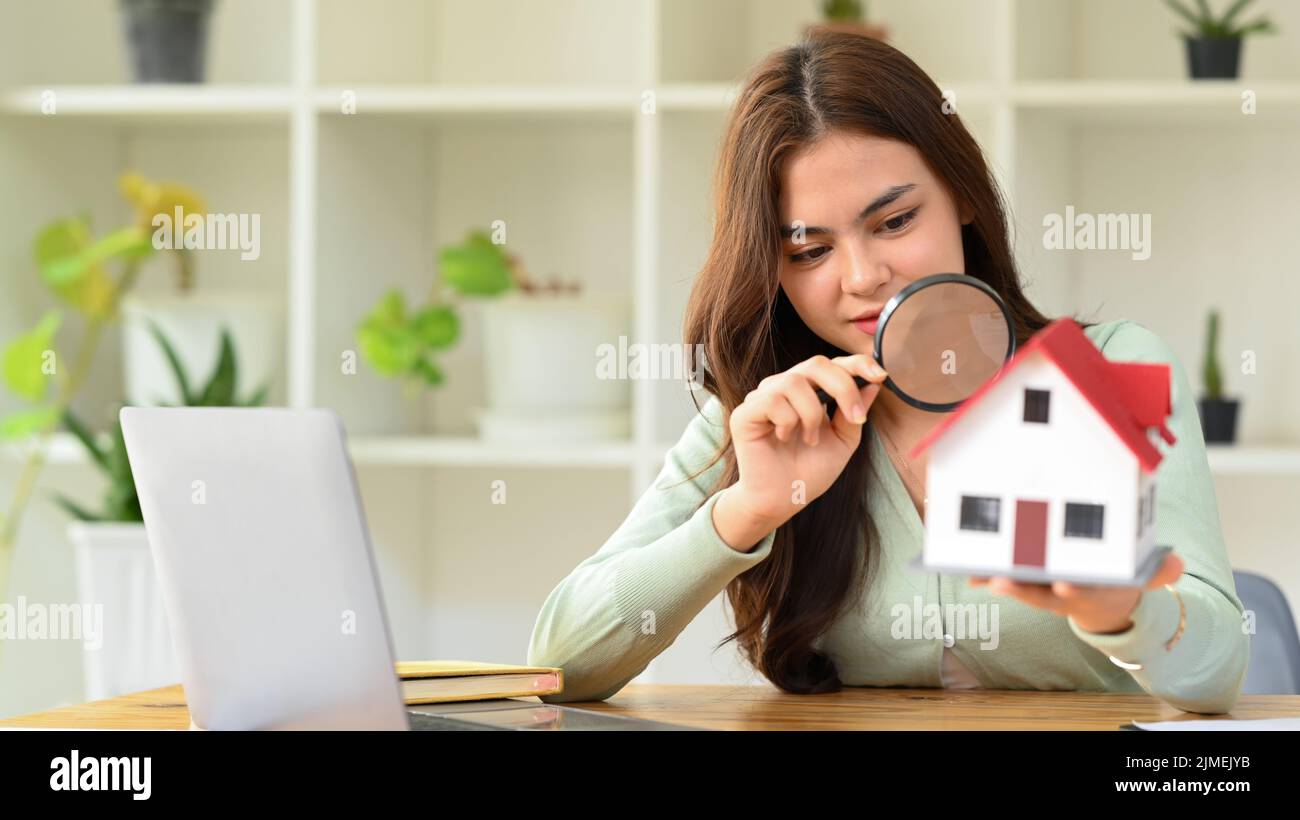 Female inspector using magnifying glass examining a house model.House ...