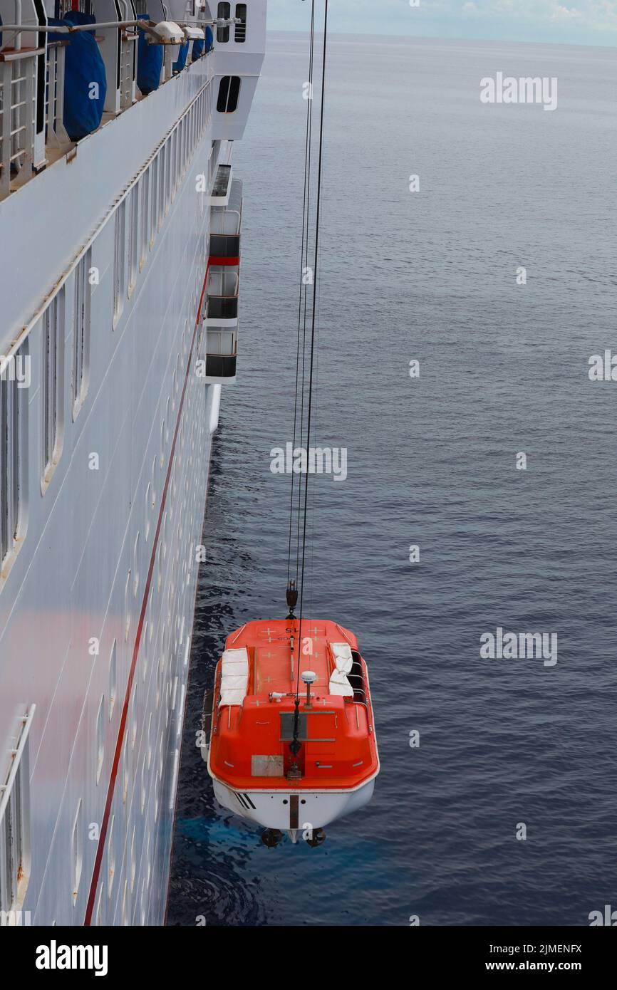 Lowering orange totally enclosed lifeboat to water. Abandon ship drill ...