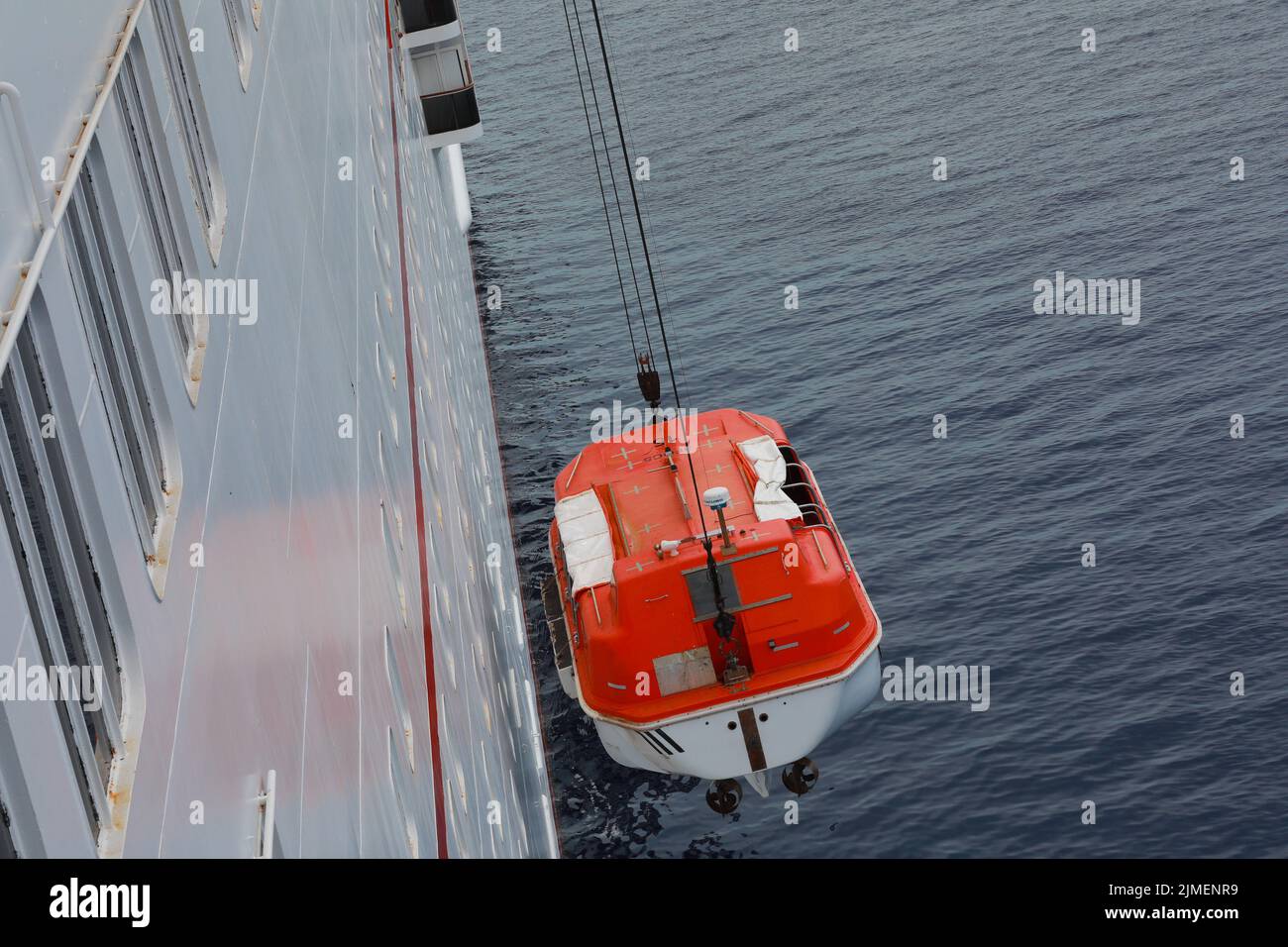 Lowering orange totally enclosed lifeboat to water. Abandon ship drill ...