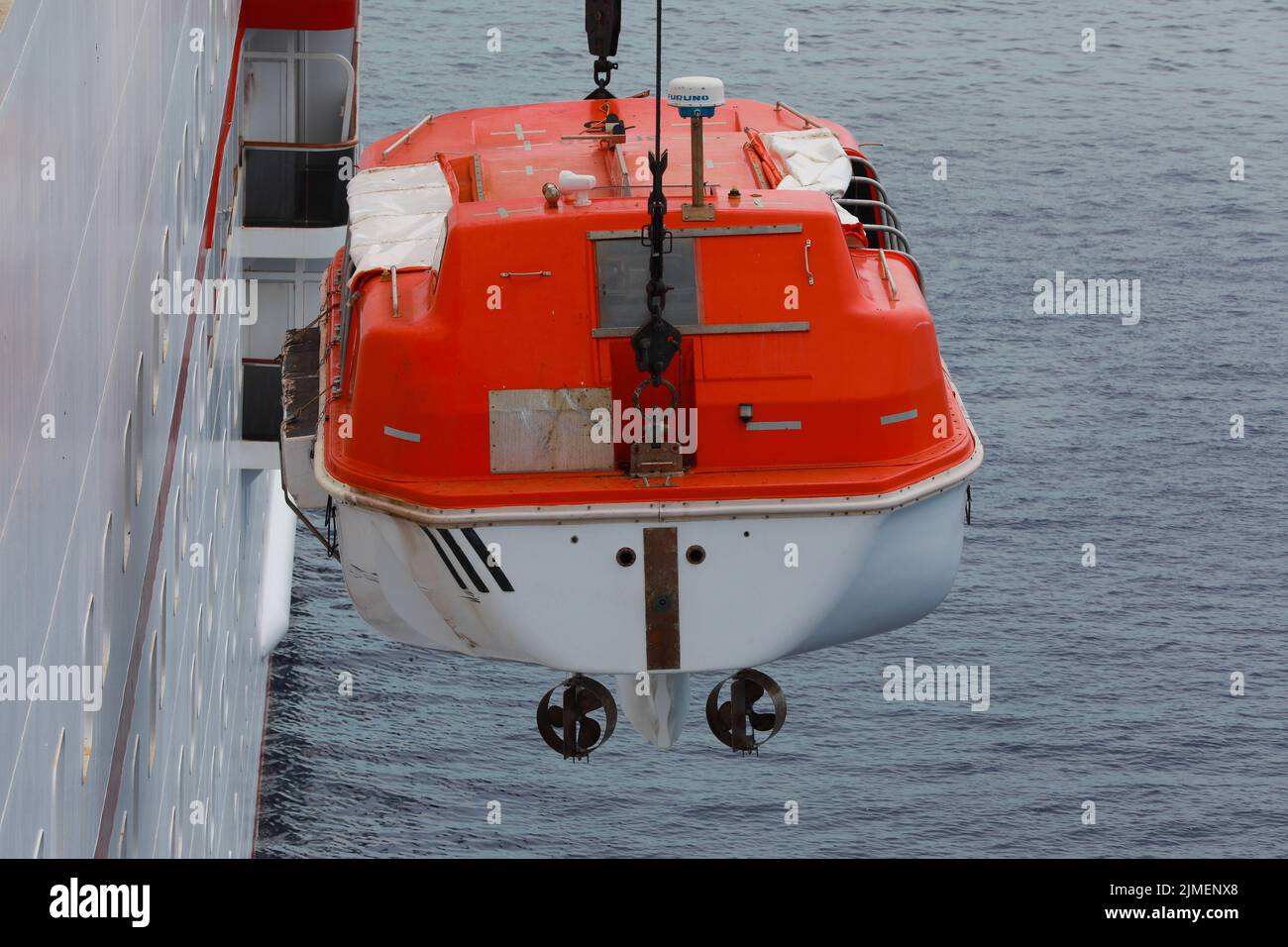 Lowering orange totally enclosed lifeboat to water. Abandon ship drill ...
