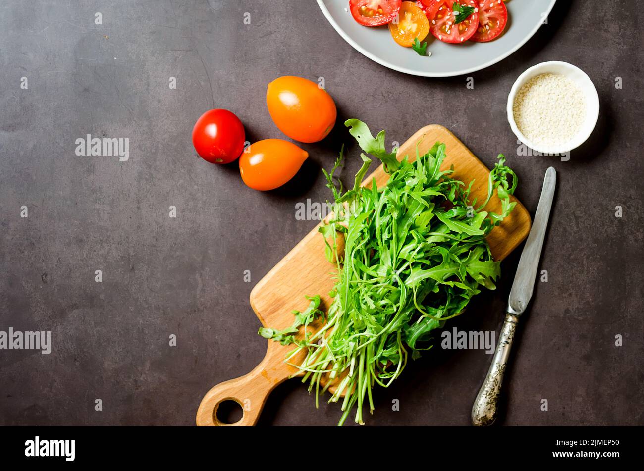 Fresh arugula on cutting board with tomatoes. ingredients for cooking ...