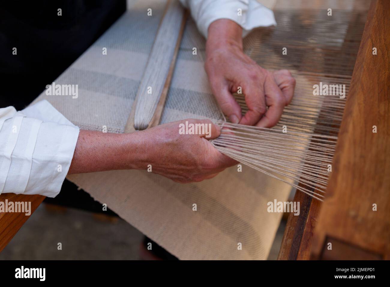 Close up on the hands of a man weaving a fabric from flax fibers with ...