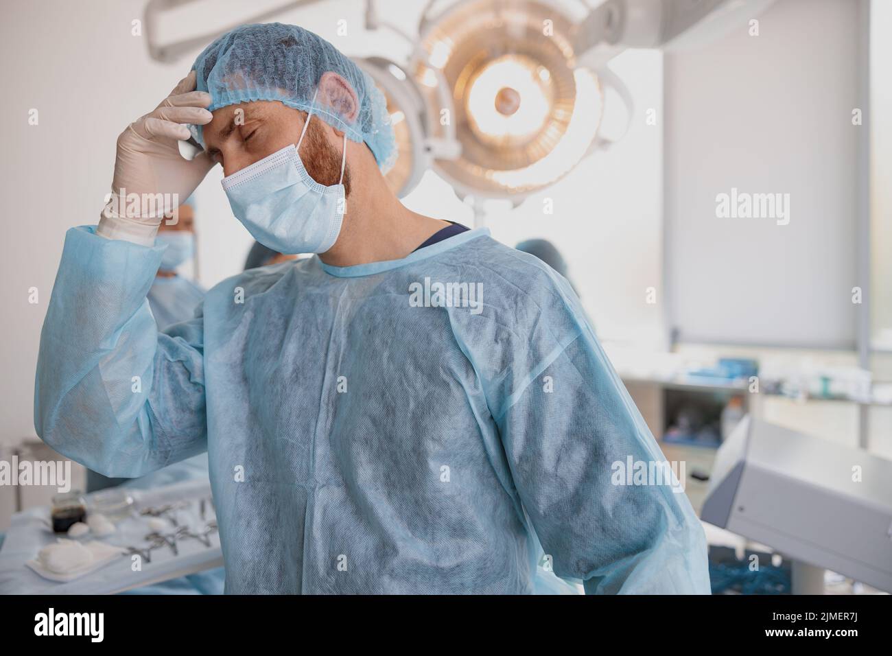 Tired professional surgeon in mask standing in operating room after ...