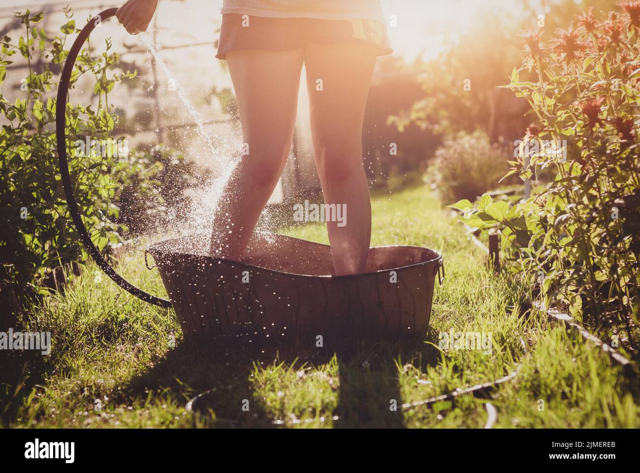 Bathing in the summer garden - woman pours cold water on her feet from ...