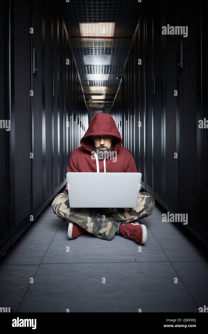 The hacker in a hood sits with the computer among servers, the burglar ...