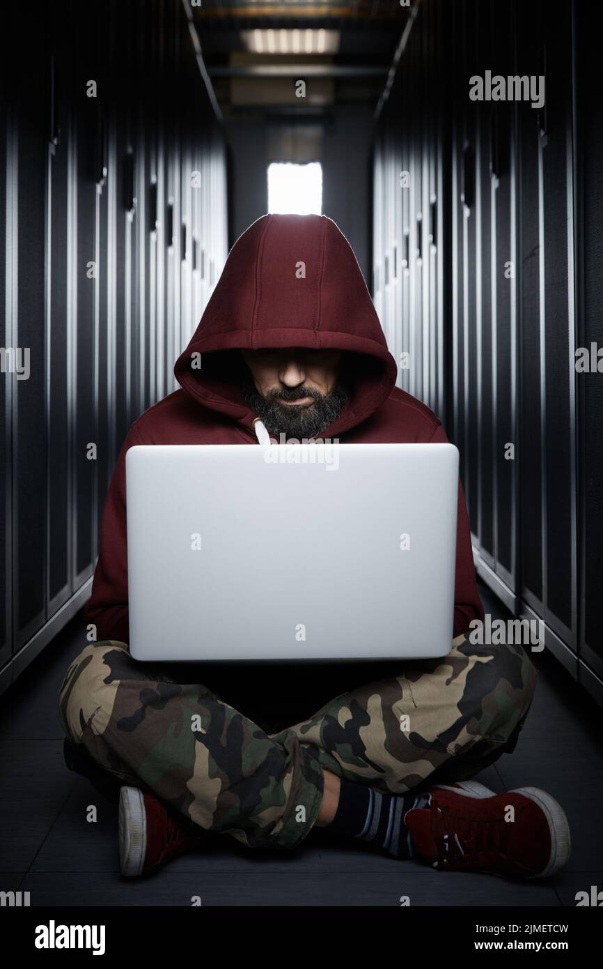 The hacker in a hood sits with the computer among servers, the burglar ...