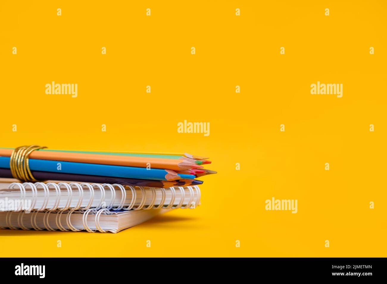 Colored pencils on a stack of notebooks on a yellow background with ...
