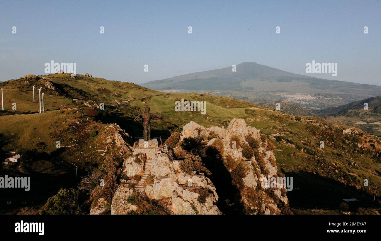 The aerial view of a bronze man sculpture on top of the hill under the ...
