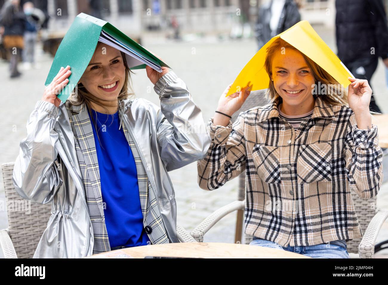 Two female students sitting outside at a terrace table covering their ...