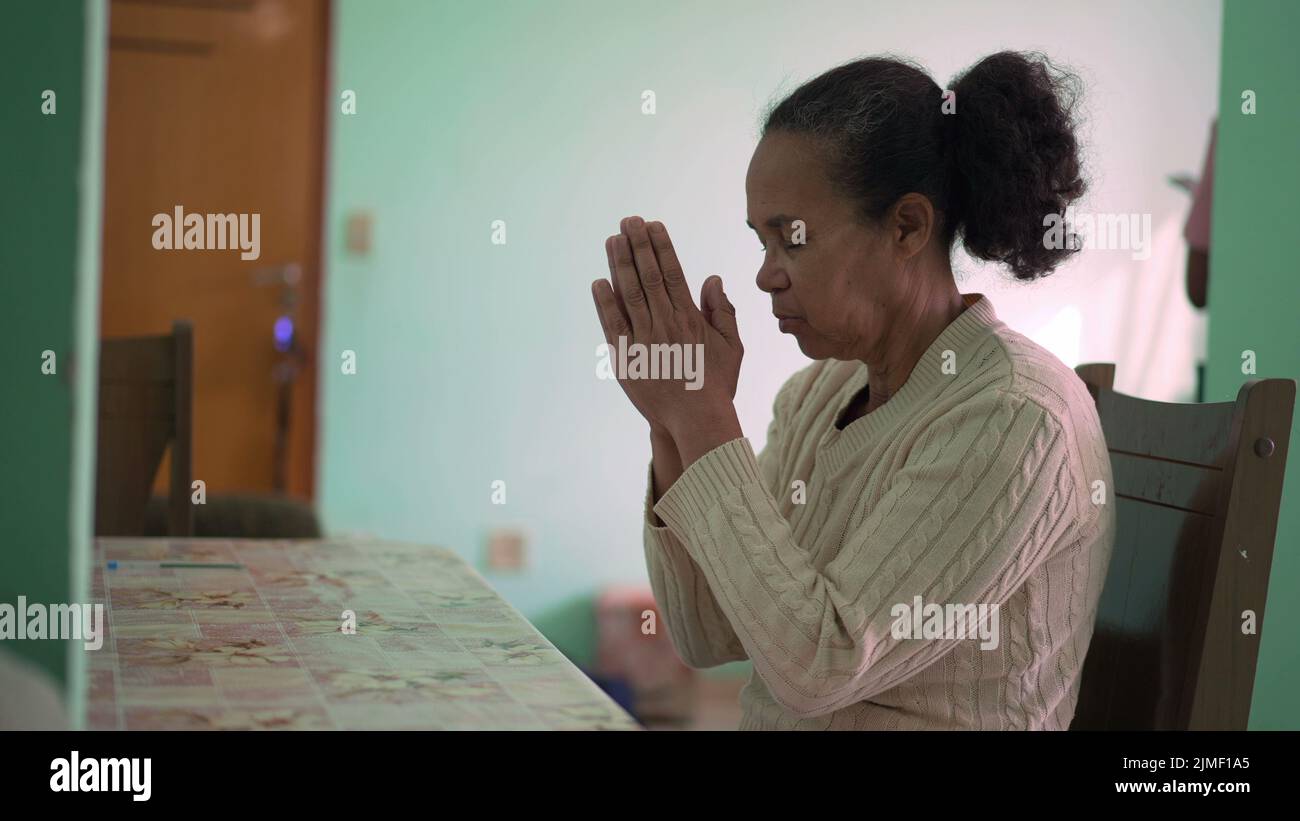 Contemplative senior person praying at home. One hopeful older black ...