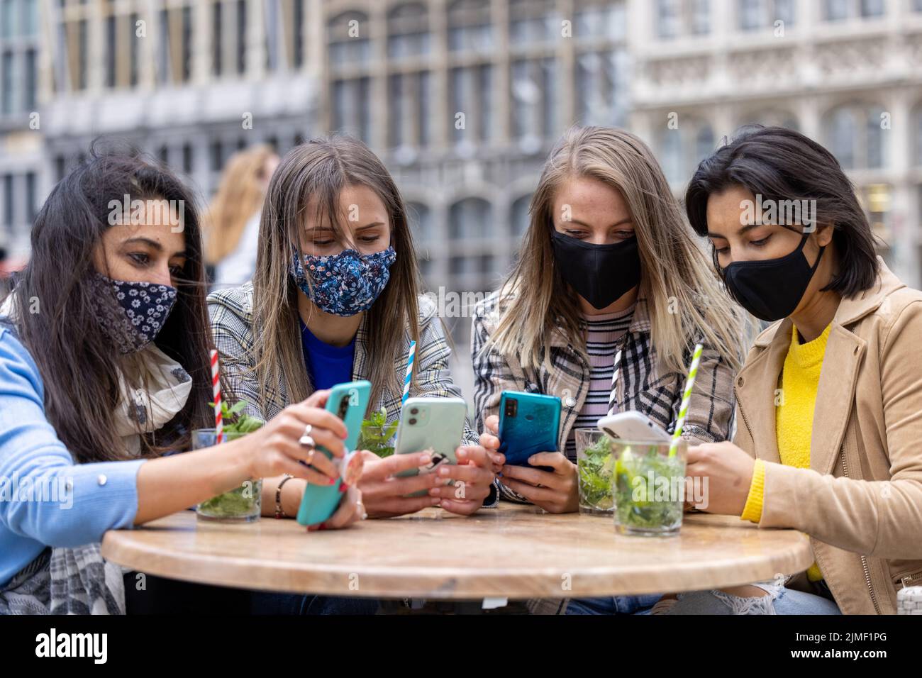 Multiracial Young Female Friends Wearing Facemasks Using Mobile