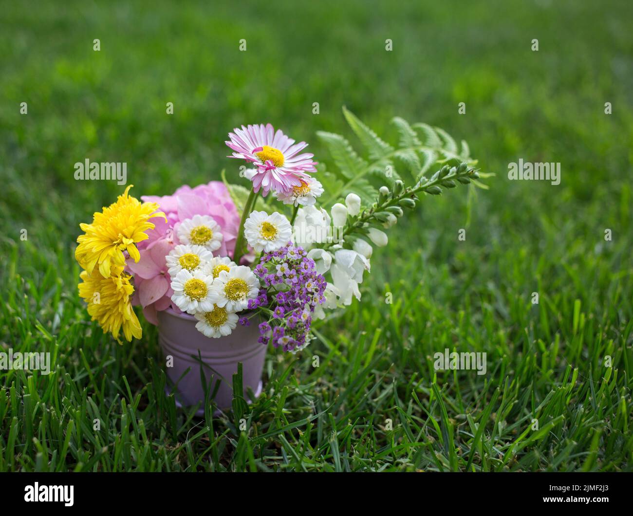 summer flower bouquet of various flowers in a small metal bucket stands ...
