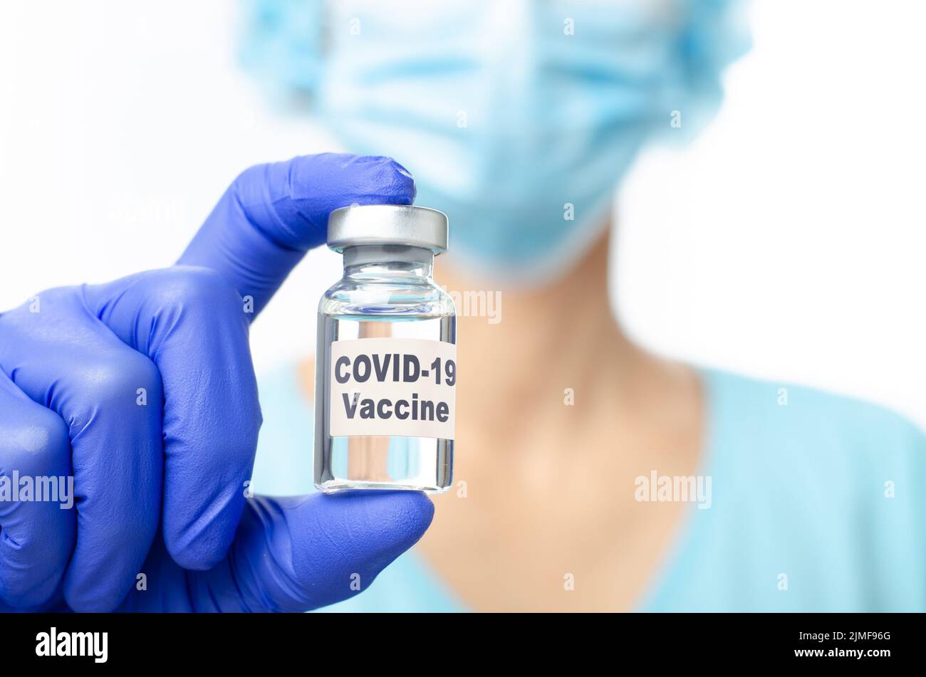 Middle age female nurse in safety mask and gloves holds bottle with ...
