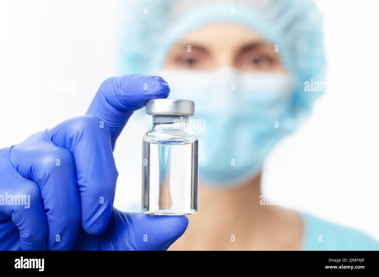Middle age female nurse in safety mask and gloves holds bottle with ...
