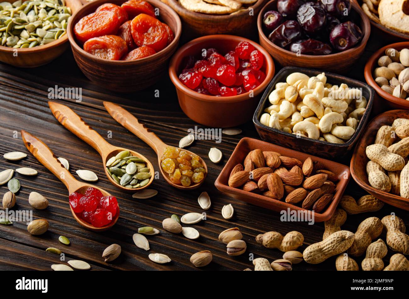 Nuts seeds and dried fruits in bowls and spoons on wooden kitchen table ...