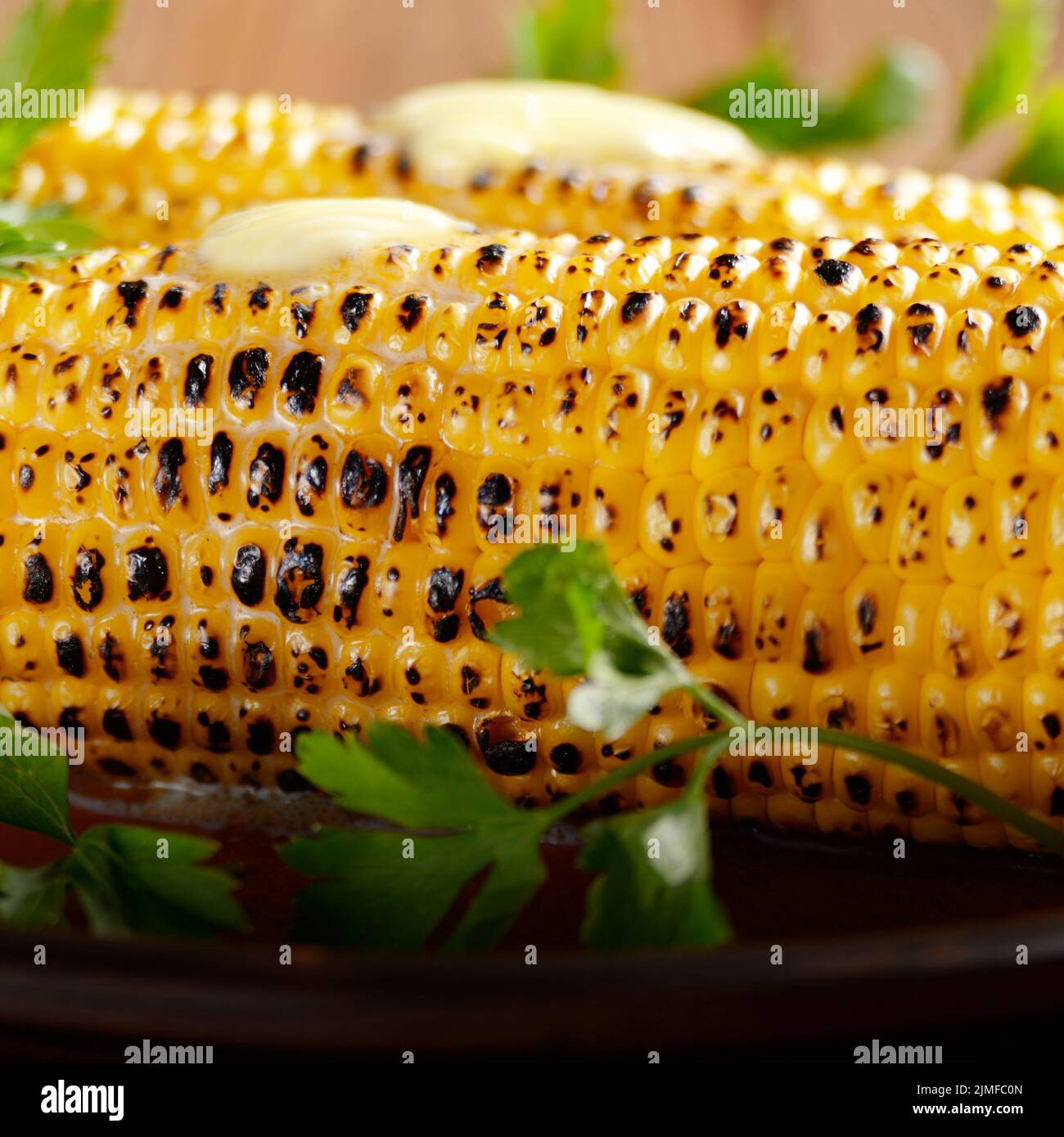 Grilled sweet corn cob with melting butter and greens on clay dish ...