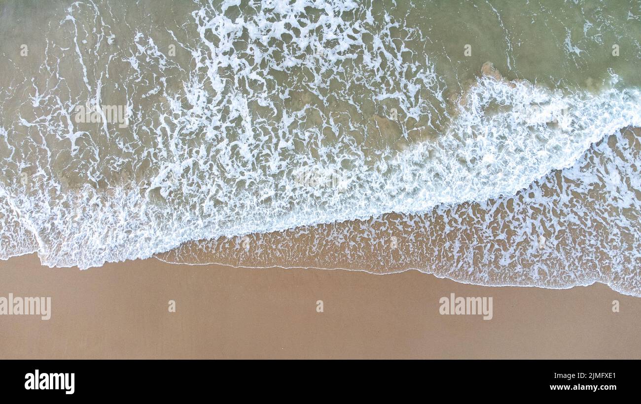Aerial drone view perpendicular to the blue waves crashing on the sandy ...