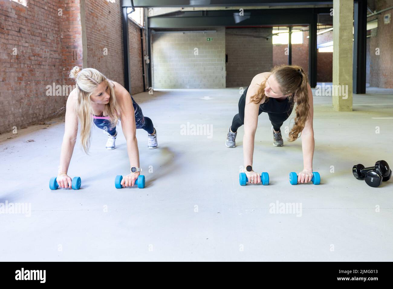 Two young attractive women doing push ups inside with barbells. Fitness ...