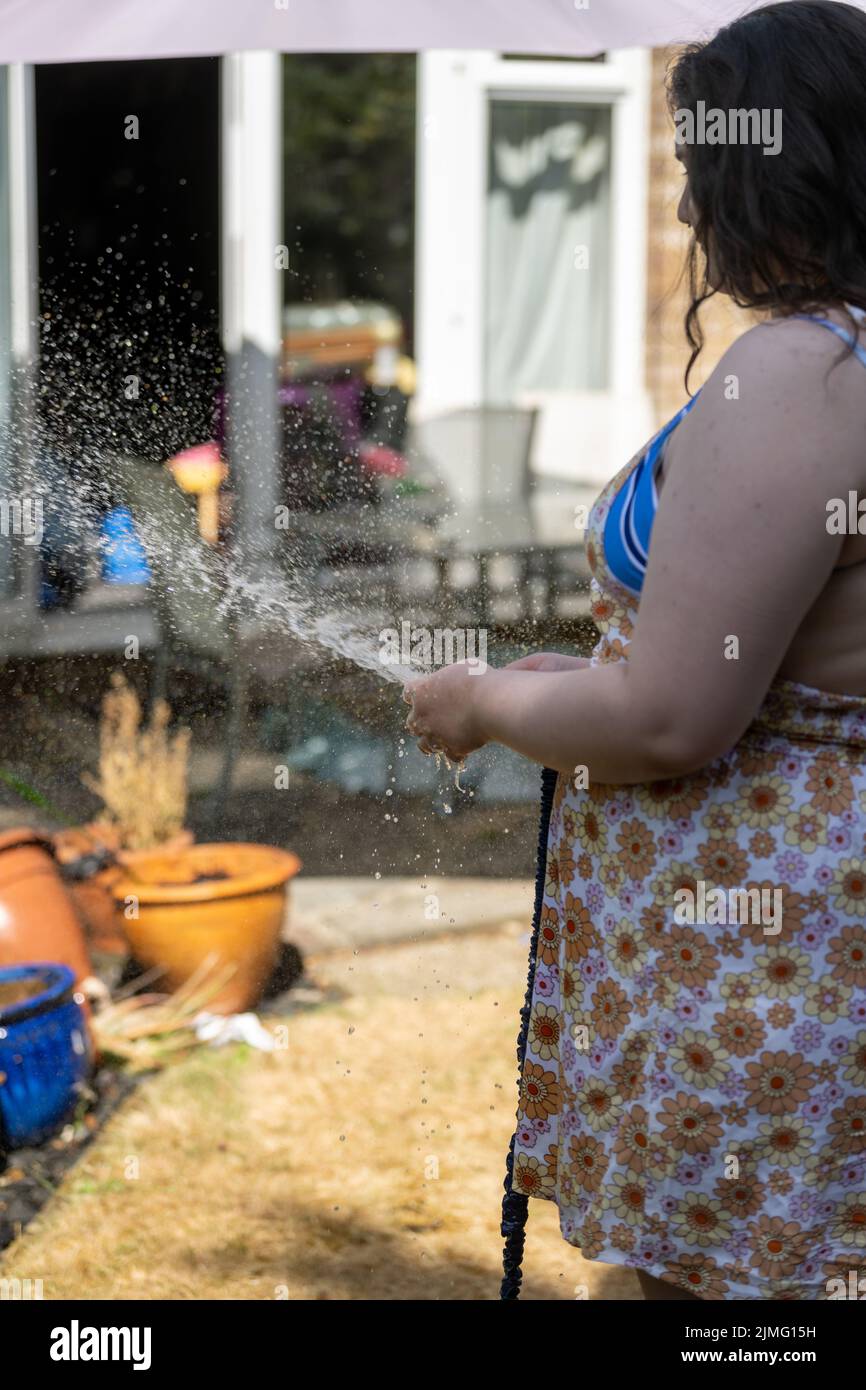 Young Woman waters garden with a hosepipe before the hosepipe ban comes ...
